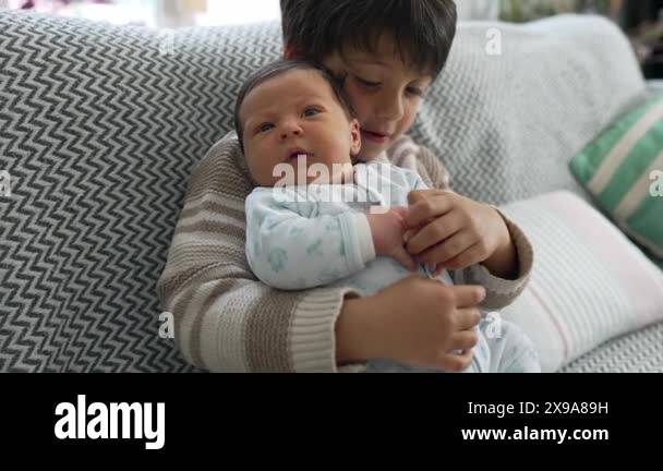 Young boy holding newborn baby, both sitting on a sofa. baby looks ...