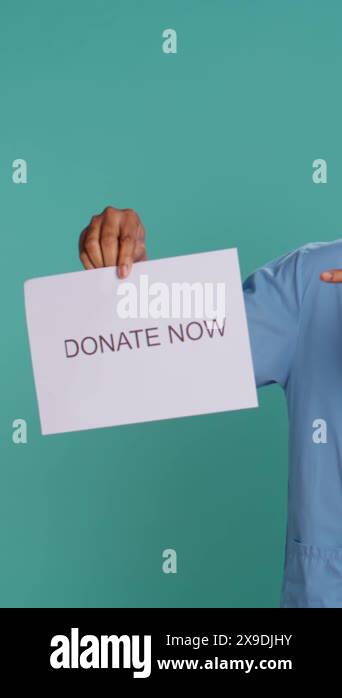 Vertical video Portrait of smiling medic holding donate now sign ... Vertical video Portrait of smiling medic holding donate now sign ...