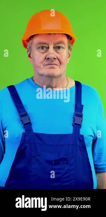 Senior worker in overalls and helmet looking at camera and smiling ...