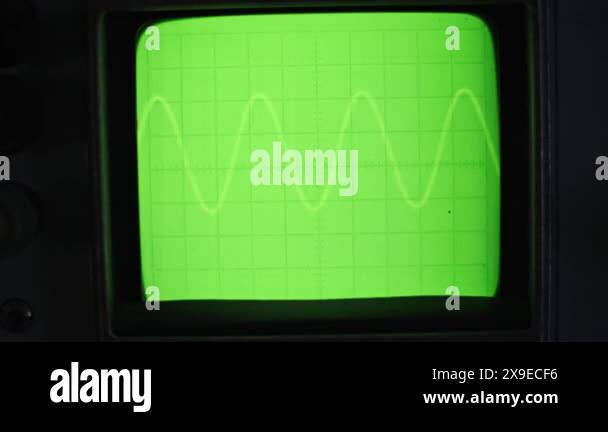 A vintage oscilloscope displays green waveforms on its CRT. The signal ...