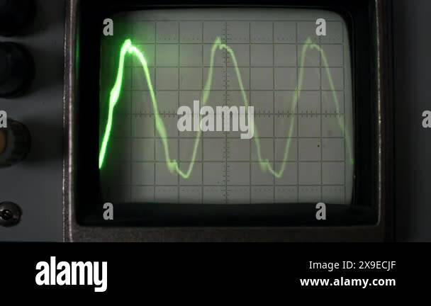 A vintage oscilloscope shows a steady green signal waveform on its ...