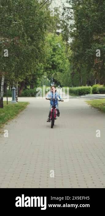 Vertical screen: Smiling girl enjoys solo bike ride down tree-lined ...
