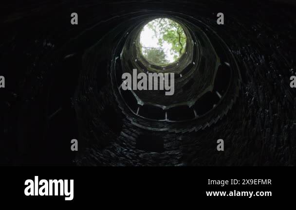 Looking up from the base of a moss-covered stone well, with a view of ...