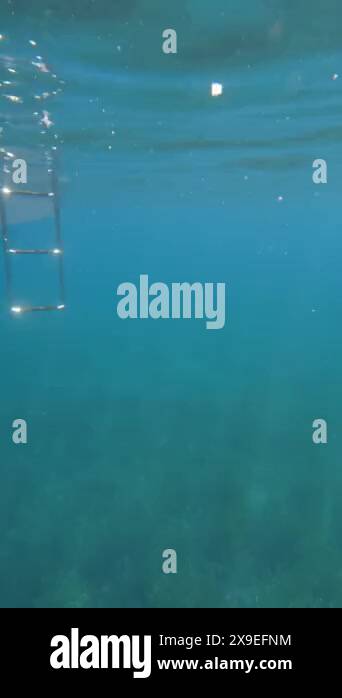 Vertical video of a teenage boy swimming underwater beneath a yacht and ...