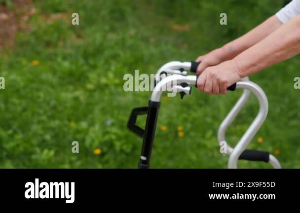 A close-up of an elderly womans hands gripping a walker in a lush green ...