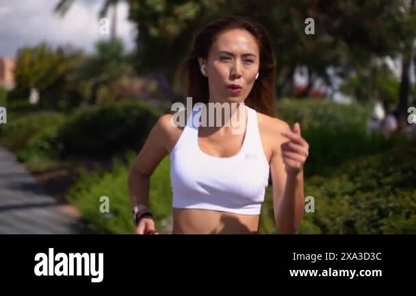Asian oriental adult woman jogger in sportswear running workout sunny morning urban high tech ...
