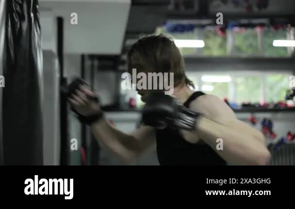 Sweaty male with long hair practicing punch combinations on leather ...