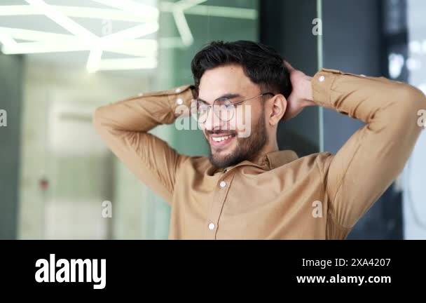 Happy businessman relaxes with hands behind head sitting at workplace ...