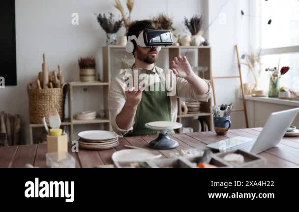 Man wearing VR headset sculpts clay vase in cozy pottery studio. Scene ...