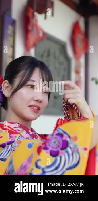 A young woman in traditional Ryuso attire captures a selfie in a ...