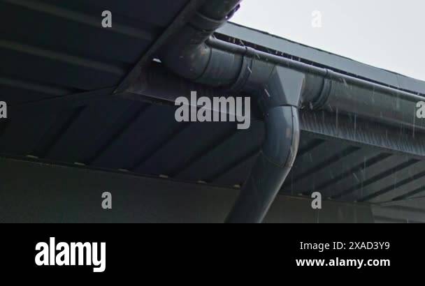 A roof with a gutter system and downspout is seen under heavy rain ...