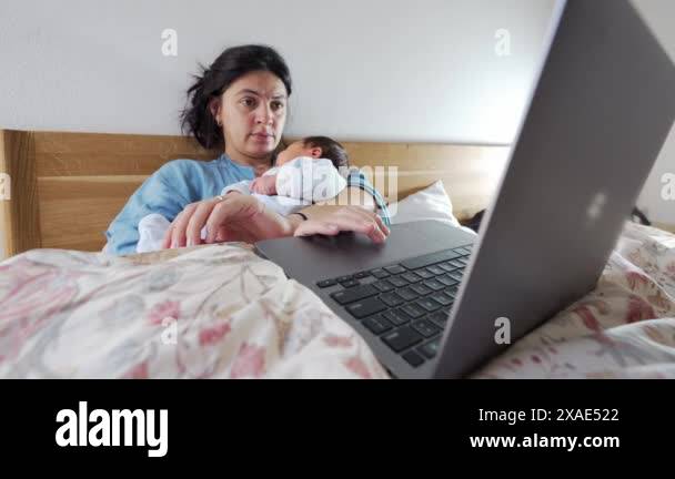 Mother working from bed with newborn baby, showcasing the challenges ...