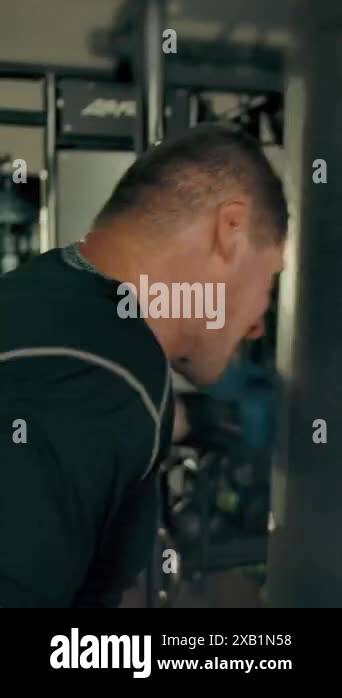 Strong man hitting punching bag indoor of modern gym. Back side view ...