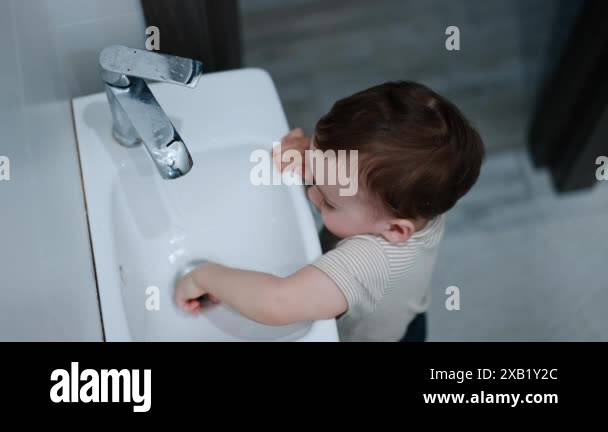 Adorable little boy plays in the sink. Kid touches the drain hole and ...