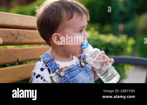Cute boy opens mouth wide to catch the bottle and drink some water ...