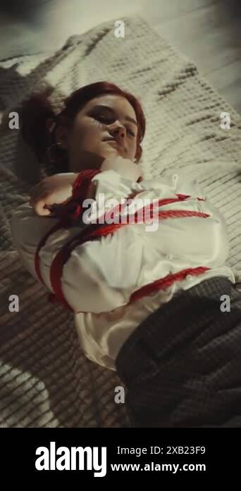 Vertical screen: Young woman lying on white textured blanket in shibari ...