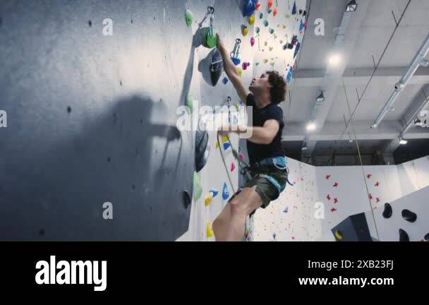 A determined climber is scaling a vertical wall, gripping green holds ...