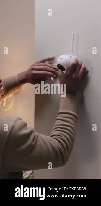 African American man puts security camera on wall mount and connects it ...