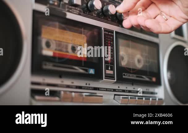 A hand adjusts the knobs on a vintage boombox, fine-tuning the audio as ...