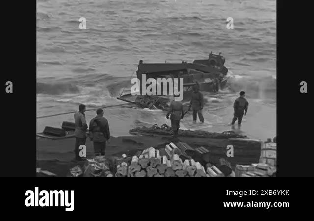 1944 - US soldiers pull loaded trailers from a landing craft onto the Attu Island beach with ...