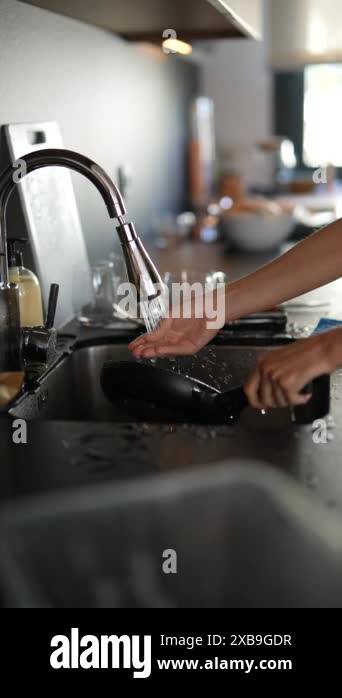 Hands washing dishes in a modern kitchen sink under running water ...