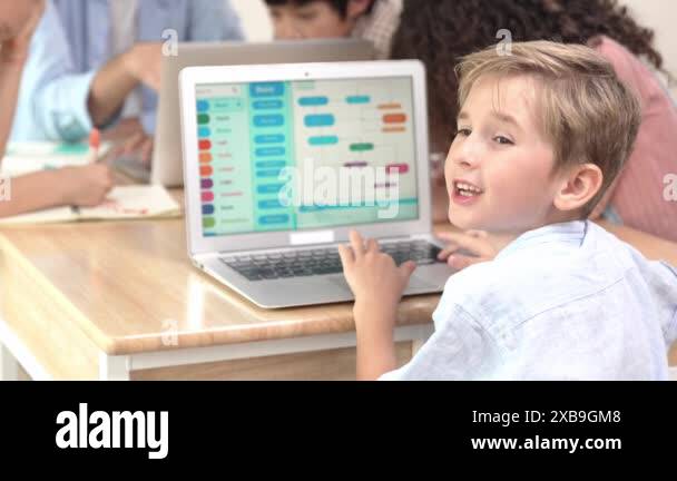 Smart caucasian boy turn around and looking at camera in STEM technology class while group of ...