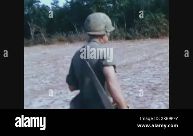 American soldiers walk between trees on a Vietnamese rubber plantation ...