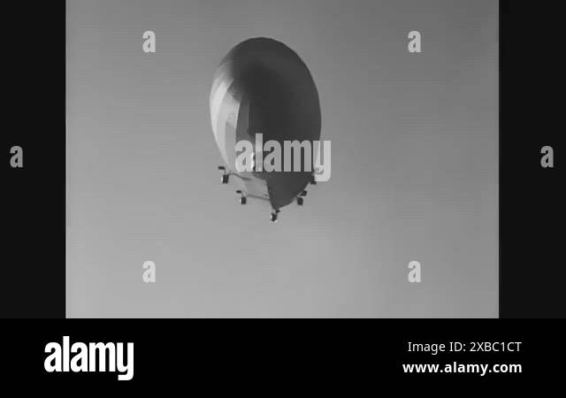 1928 - Men watch the dirigible USS Los Angeles hover over the USS Saratoga aircraft carrier ...