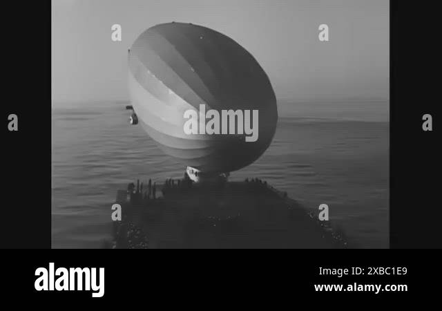 1928 - Men haul on the lines of the dirigible USS Los Angeles and pull it toward the deck of the ...