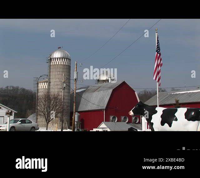 The camera captures an American farm with silos, red barn, American ...