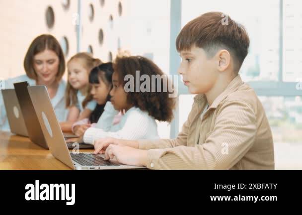 Boy playing laptop with multicultural friend learning prompt at STEM technology class ...