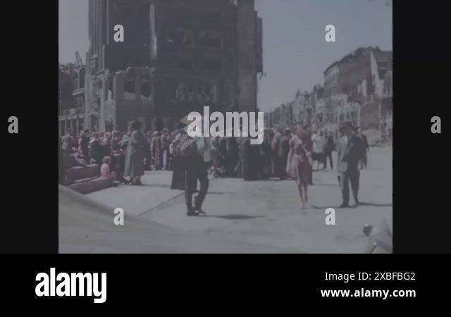 1945 - Berlin civilians wait for a bus in their war-torn city. A mother tends to her young ...