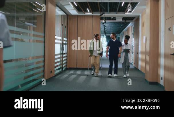 Man on crutches is supported and assisted by kind Caucasian nurse and a ...