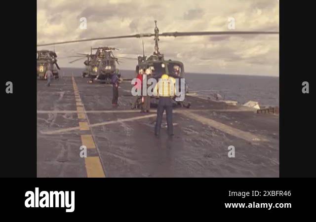 1975 - A helicopter lifts off and crew activities on deck of the USS ...
