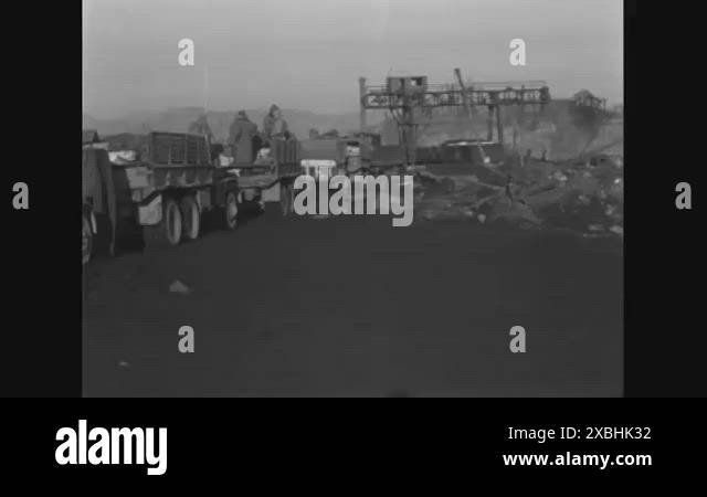 A line of trucks to be hoisted aboard and an artillery piece are shown ...