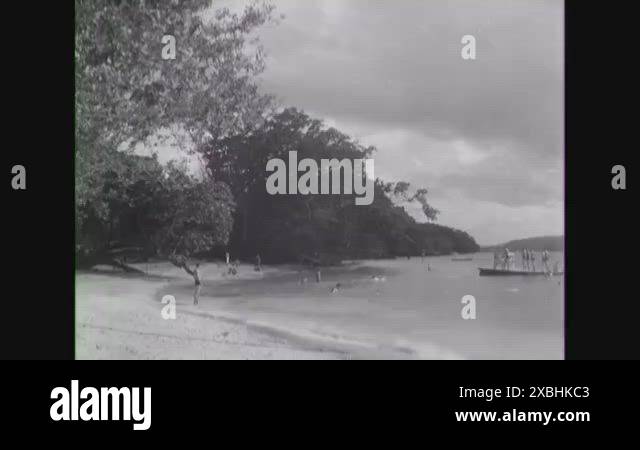 Sailors swim and wade and dive off a floating dock and a seaman wearing ...