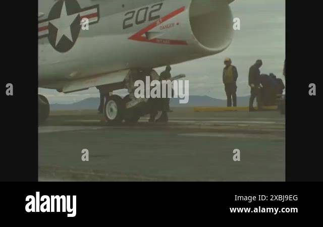 1970 - A close-up shows a US Navy plane being guided onto a catapult ...