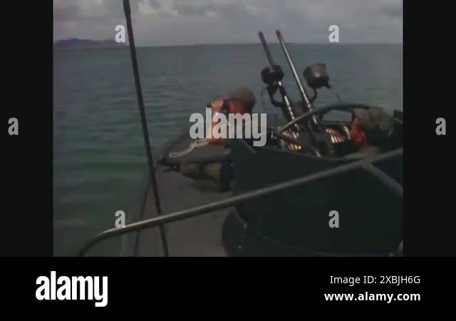 1967 - Two soldiers on a river patrol boat, one aims a machine gun the ...