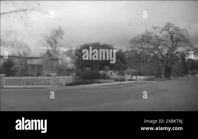 1963 - A paper boy goes about his route in a suburb; shops in town are ...