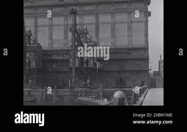 1920s - A crane is used to load cargo on to a ship, while grain from a ...