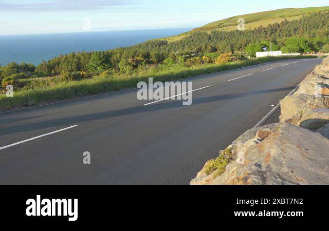 ISLE OF MAN - 8.26.2023 - Two motorcyclists drive up a road past the ...