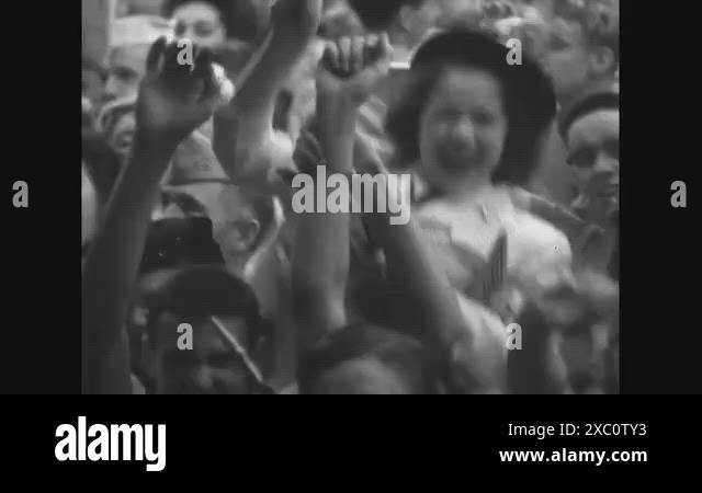 1945 - A crowd of American servicemen and civilians wave to the camera ...