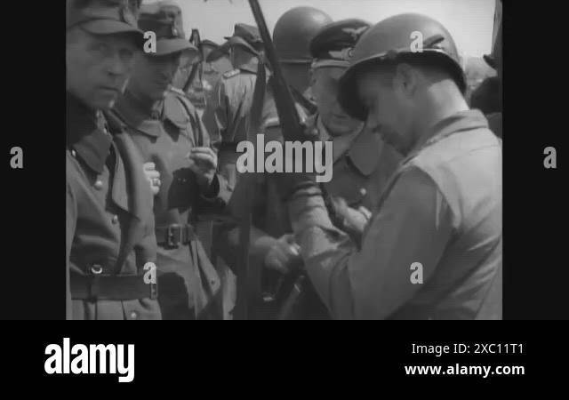 1945 - American soldiers speed German POWs along into a prison compound ...