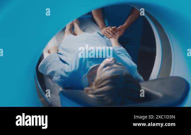 Inside view of MRI machine with female patient lying on scanner bed holding hands of partner ...