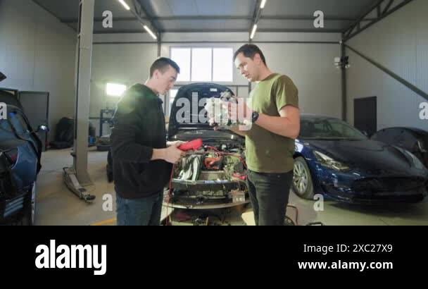 Two car mechanics working on an electric car engine in a modern auto service station. Concept of ...