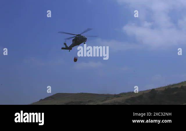 A water dropping helicopter picks up water for an airdrop during a ...