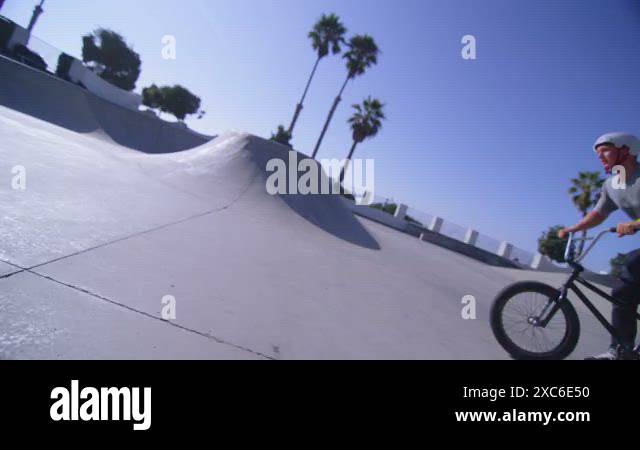 The camera follows a BMX bike rider as he jumps and rides the wall of a ...