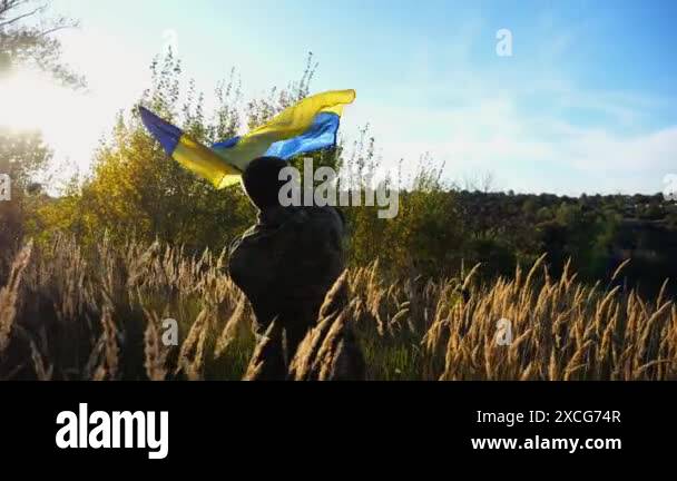 Male military in uniform waving flag of Ukraine at countryside. Young ...