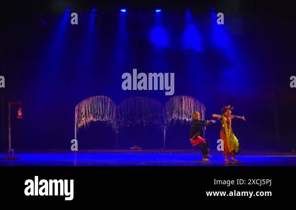 Two performers on stage under blue and yellow stage lights with a dark ...