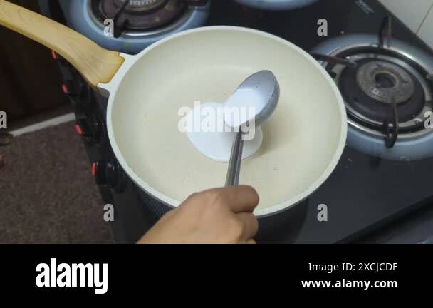 closeup a woman's hand pours white batter into a hot pan and spreading ...